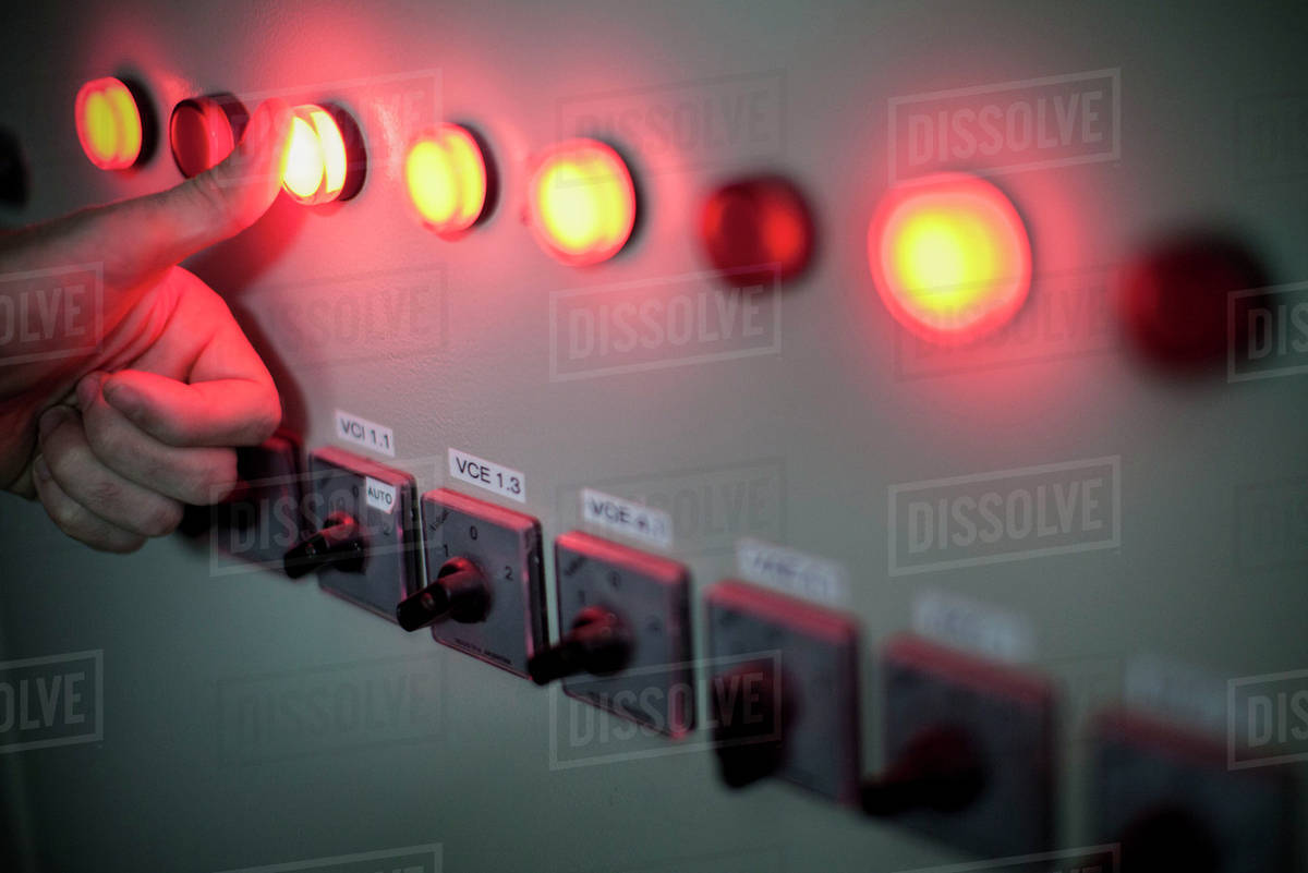 Worker pressing illuminated buttons on industrial control panel ...