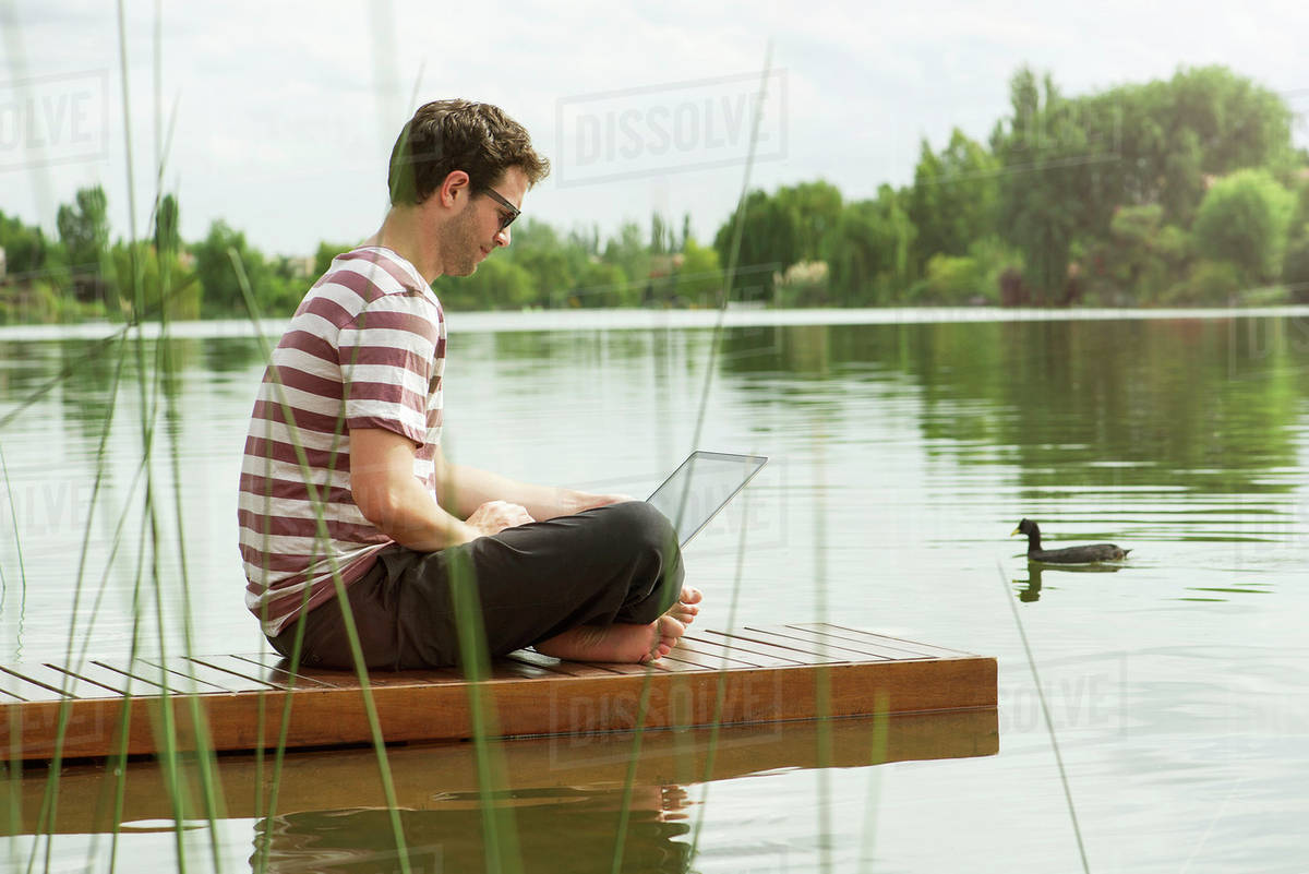Man sitting on dock using laptop computer - Royalty-free Stock Photo ...