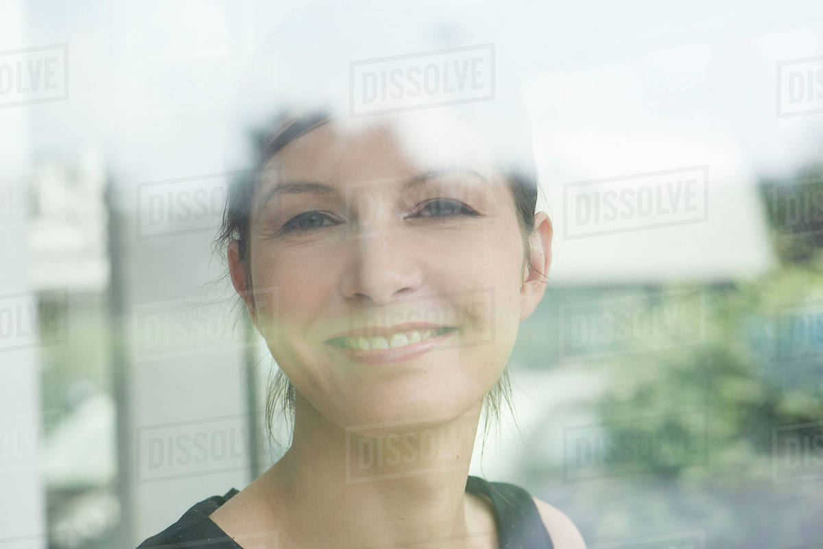 Woman looking through window, smiling, portrait - Stock Photo - Dissolve