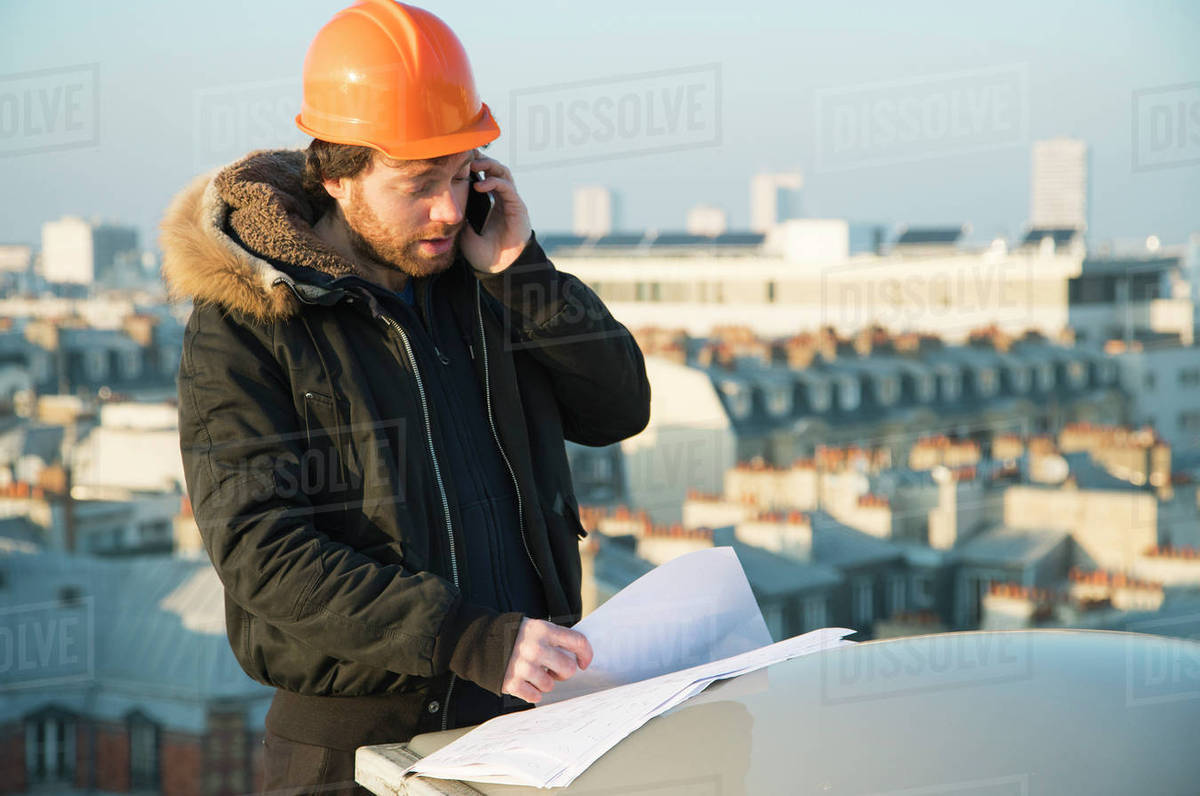 Construction supervisor studying blueprints and talking on cell phone ...