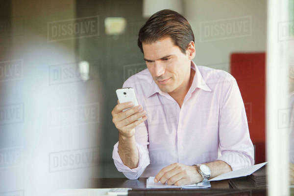 Man checking smartphone in office - Royalty-free Stock Photo | Dissolve