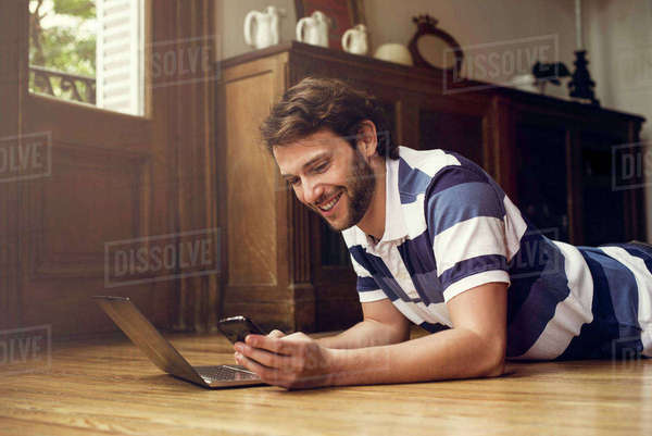Man lying on floor using laptop and smartphone - Royalty-free Stock ...