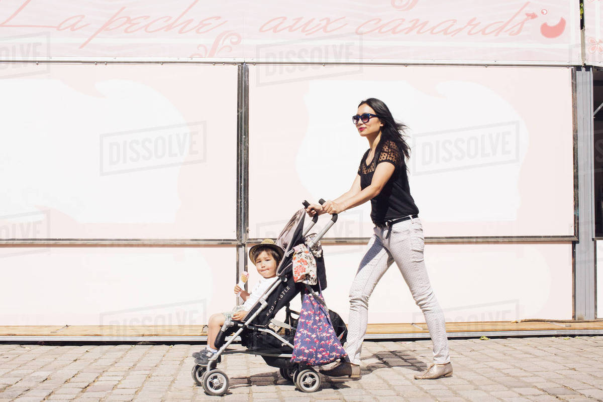 Mother pushing toddler son in stroller on sidewalk - Royalty-free Stock ...