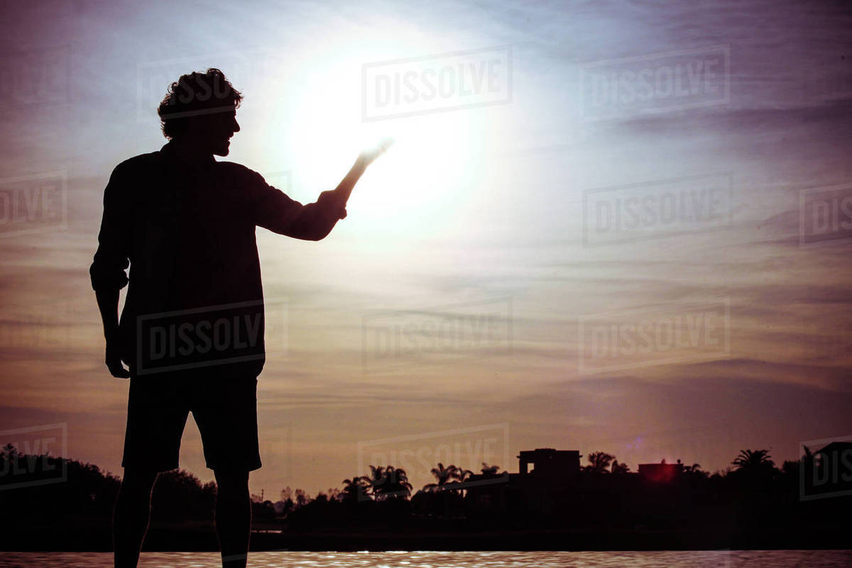 Man pretending to hold the sun at water's edge - Royalty-free Stock ...