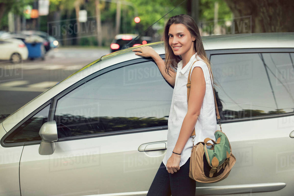 Young woman leaning against car, smiling - Stock Photo - Dissolve
