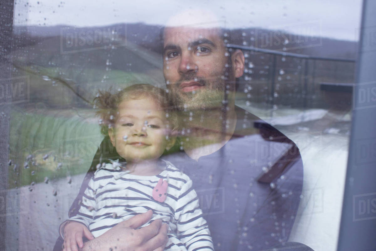 Man with young child looking through window watching rain fall - Stock ...