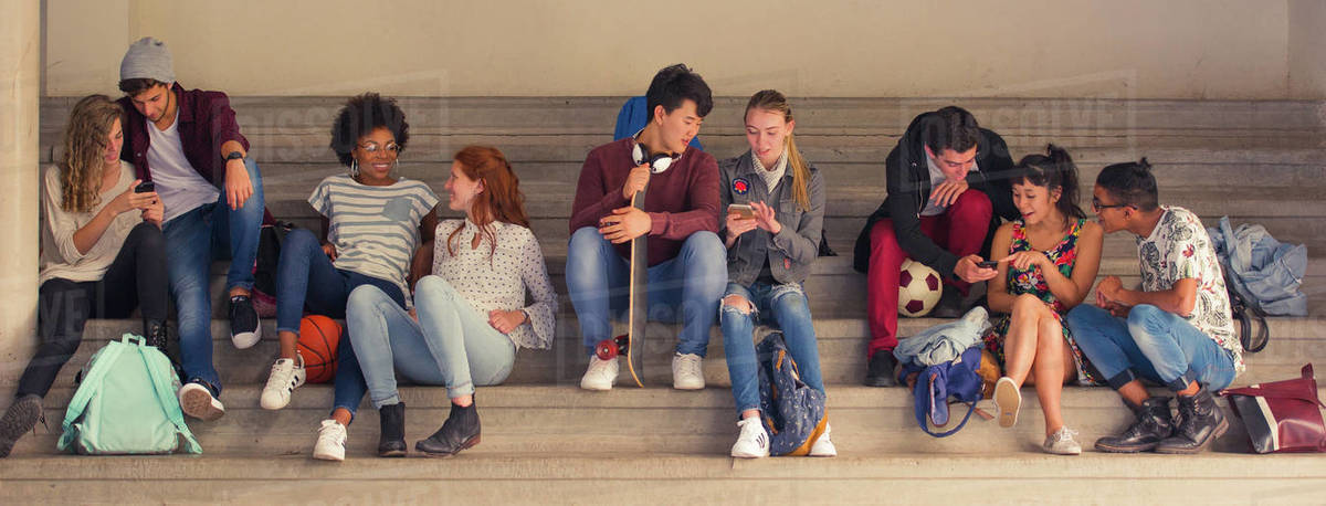 Students chatting together and looking at smartphones between classes ...