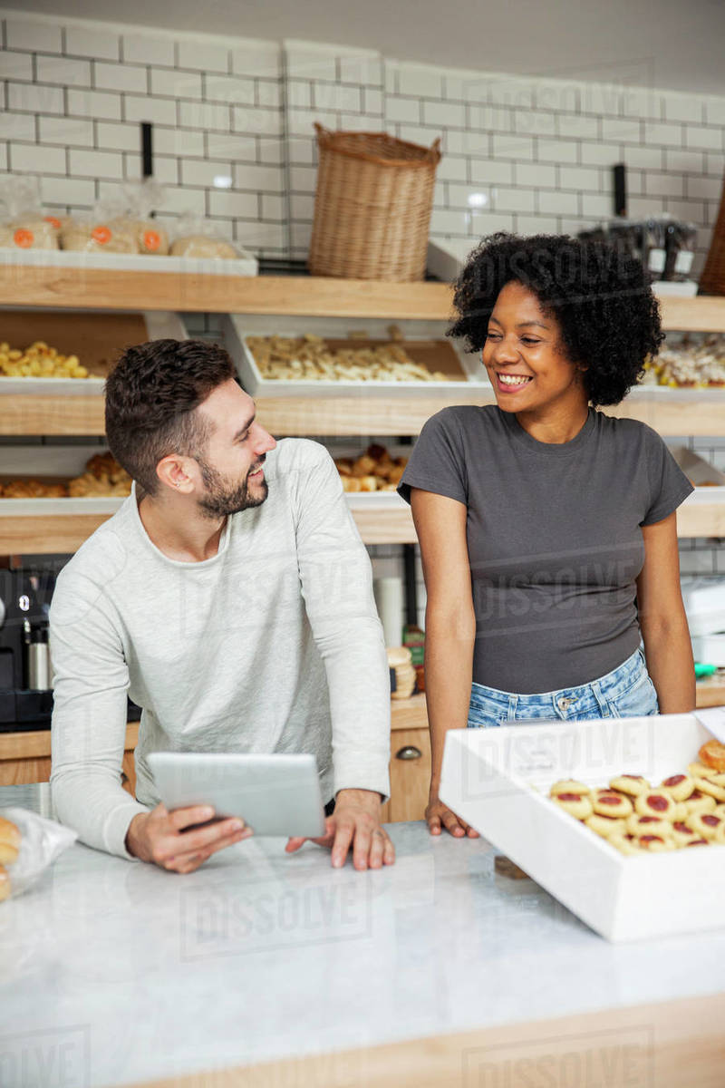 Bakery owners looking at each other while standing behind counter ...