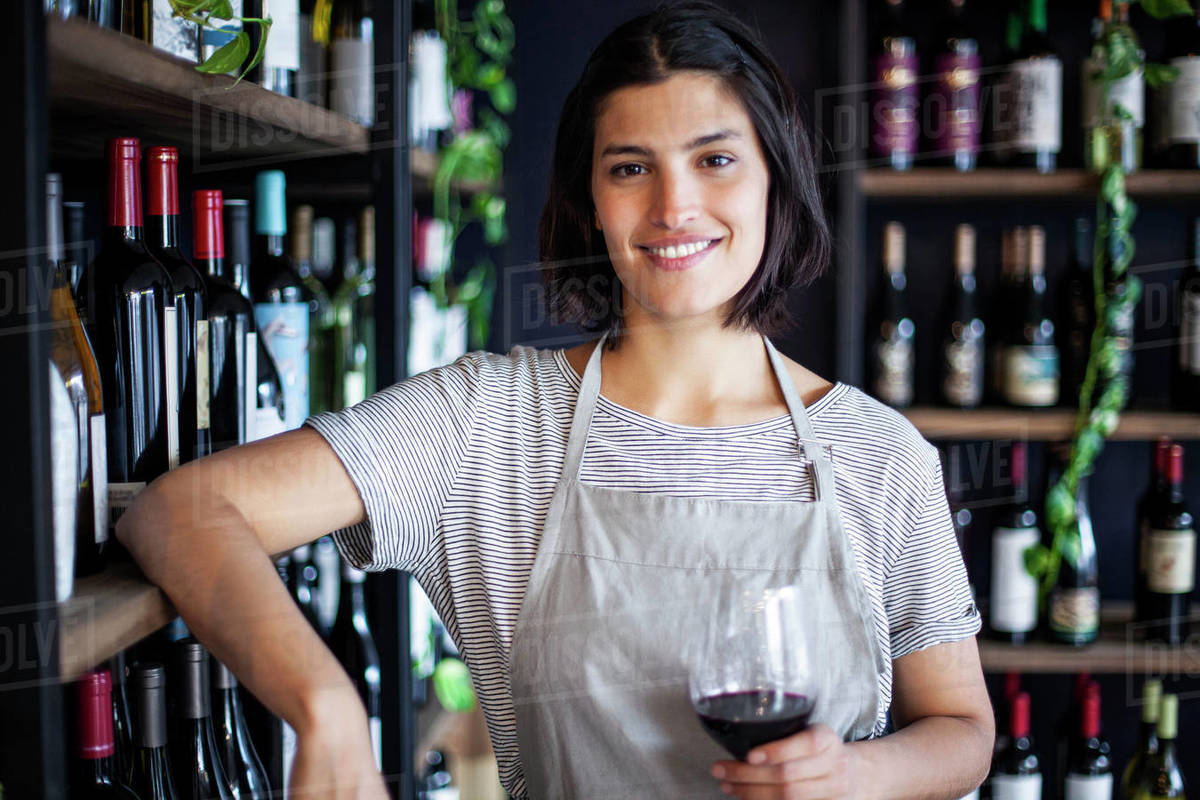 Female sommelier holding glass of wine while looking at the camera ...