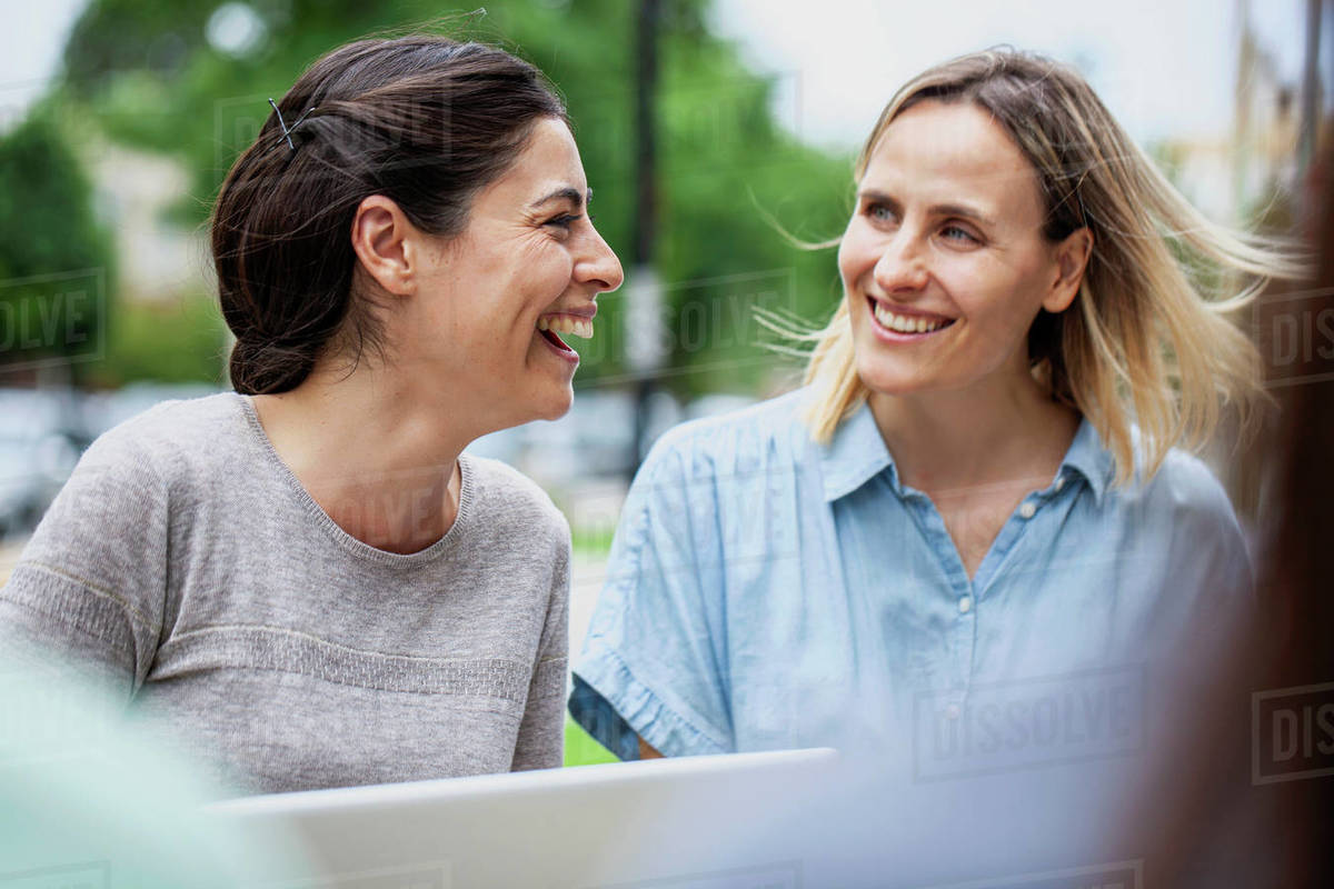 Female coworkers laughing while sitting outdoors - Royalty-free Stock ...