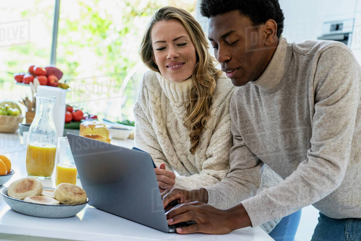 Adult man typing on laptop while leaning on kitchen counter with ...