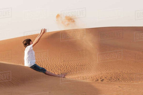 Teenage boy playfully tossing sand into air - Stock Photo - Dissolve