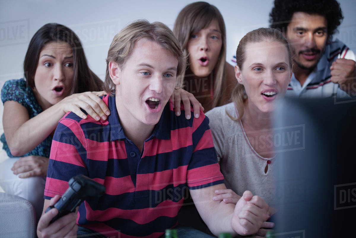 Young man playing video games while friends watch with astonishment ...