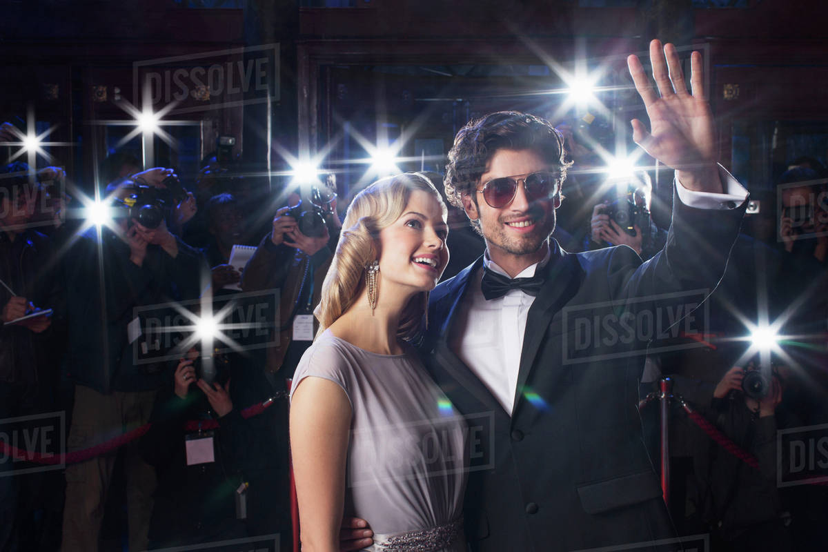 Well dressed celebrity couple waving to paparazzi at red carpet event ...