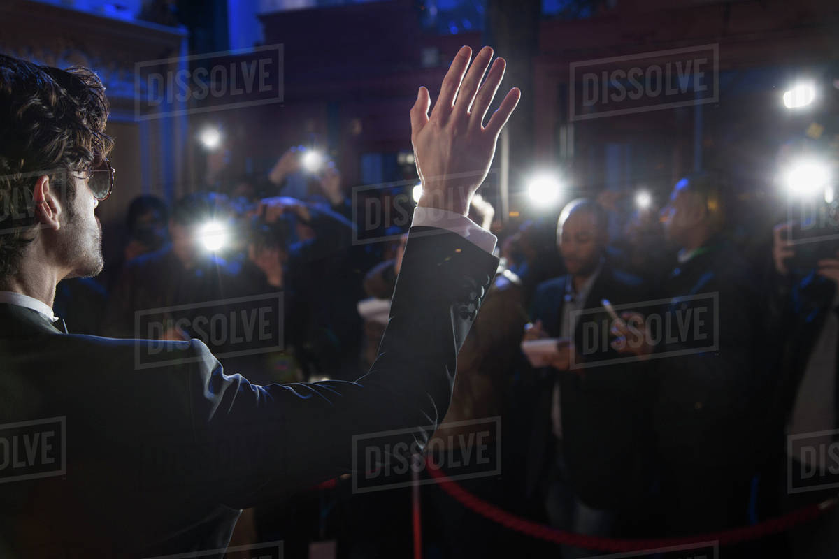 Rear view of male celebrity waving to paparazzi at red carpet event ...