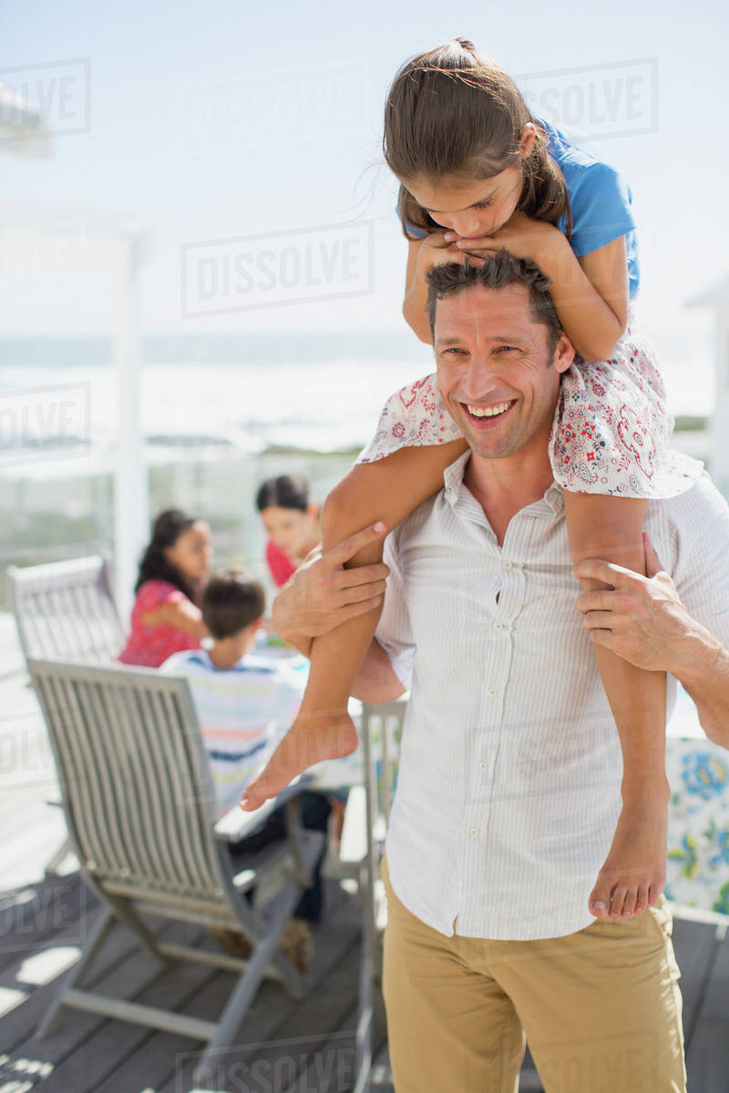 Father carrying daughter on shoulders on sunny patio - Royalty-free Stock Photo | Dissolve