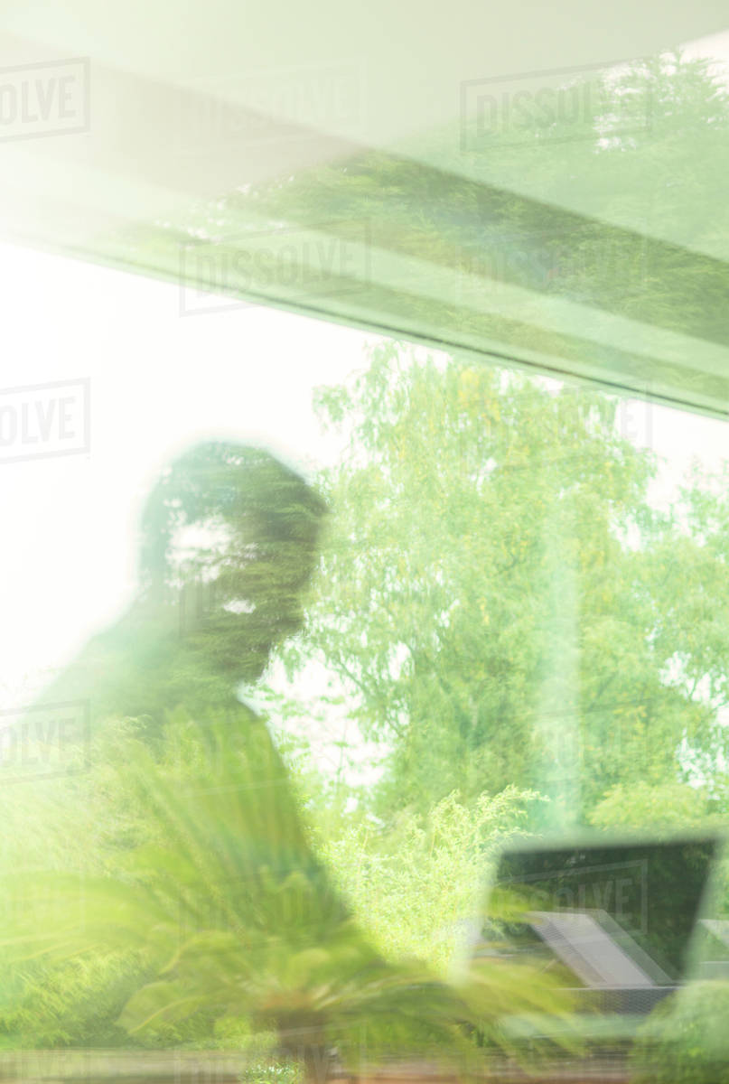 Man using laptop viewed through window - Stock Photo - Dissolve