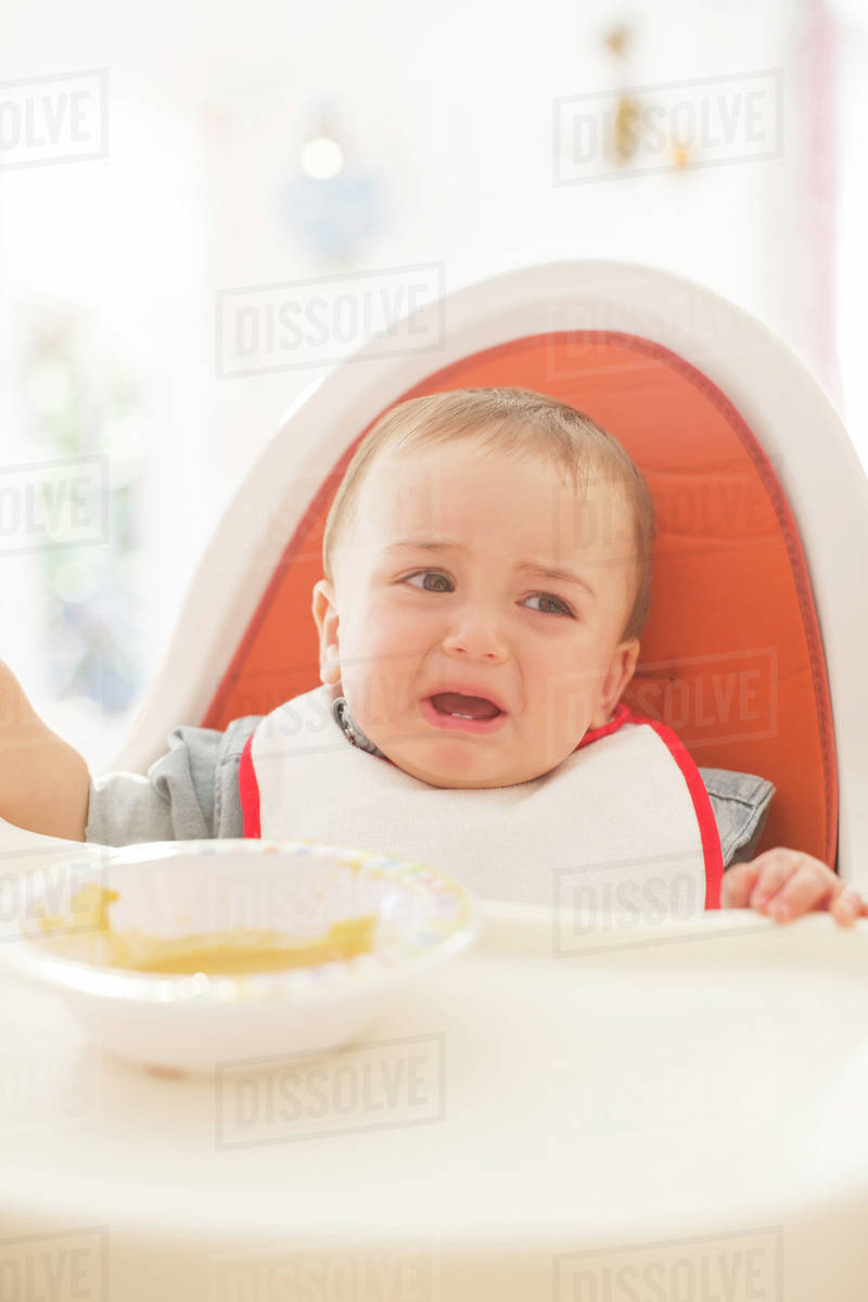 Baby boy crying in high chair - Stock Photo - Dissolve