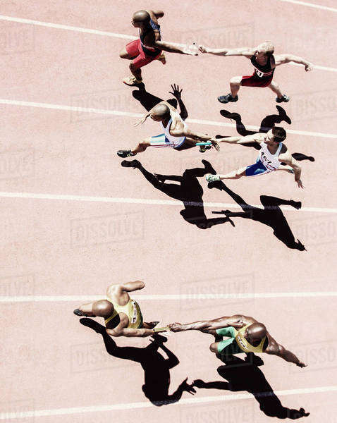 Relay runners handing off batons on track - Stock Photo - Dissolve