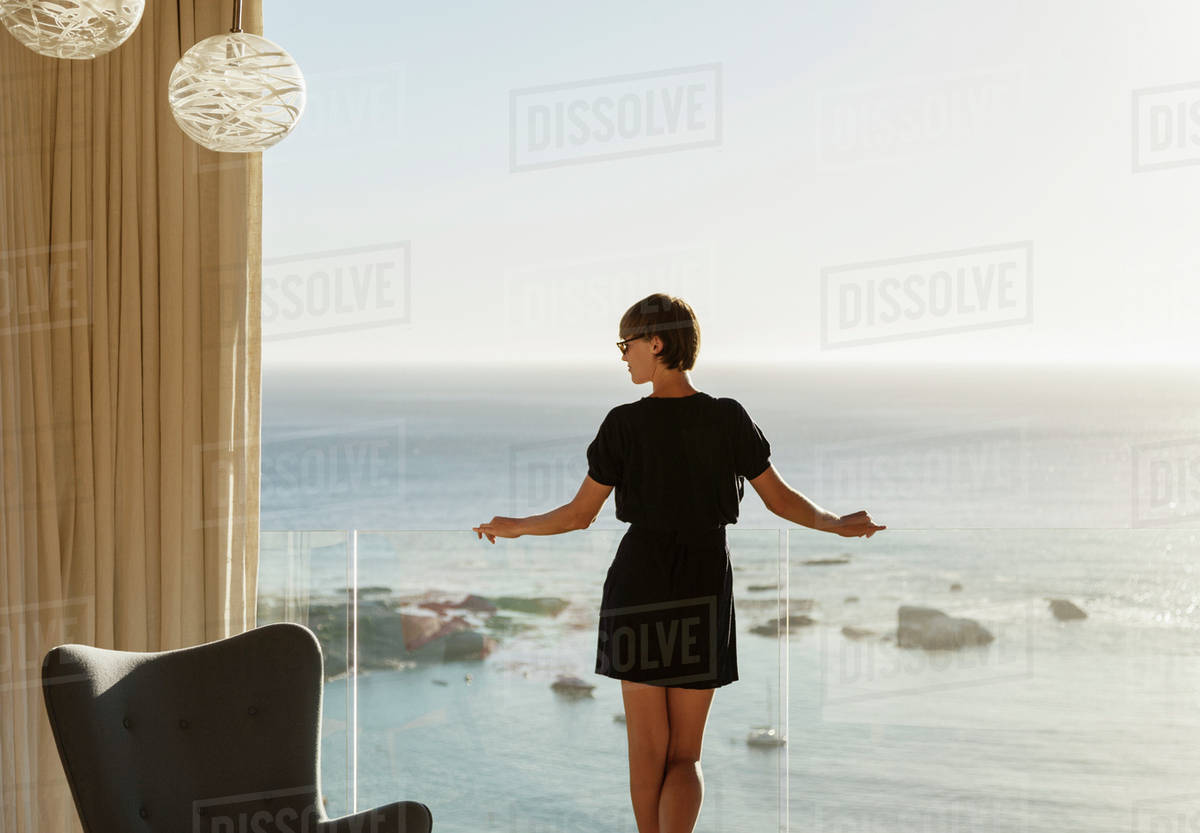 Woman standing at balcony railing overlooking ocean - Royalty-free ...