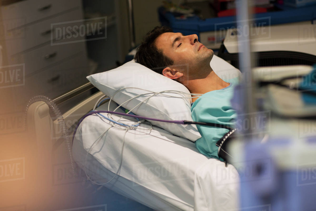 Patient attached to medical monitoring equipment lying in bed in ...
