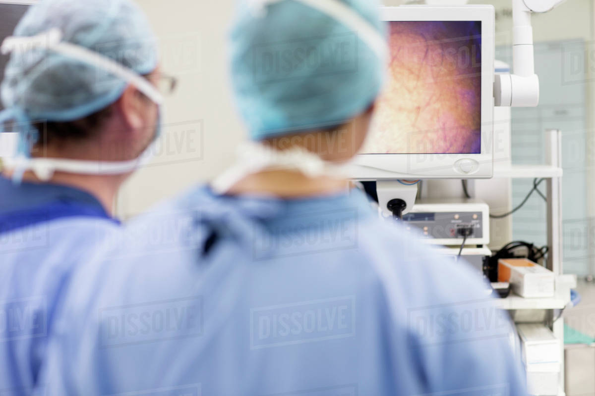 Rear view of two surgeons looking at monitor during surgery in ...
