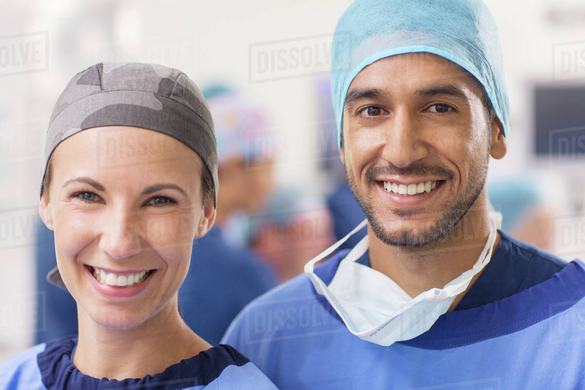 Portrait of smiling doctors wearing surgical caps in operating theater ...