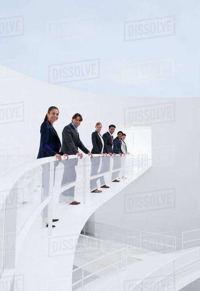 Portrait of smiling business people leaning on railing of elevated ...