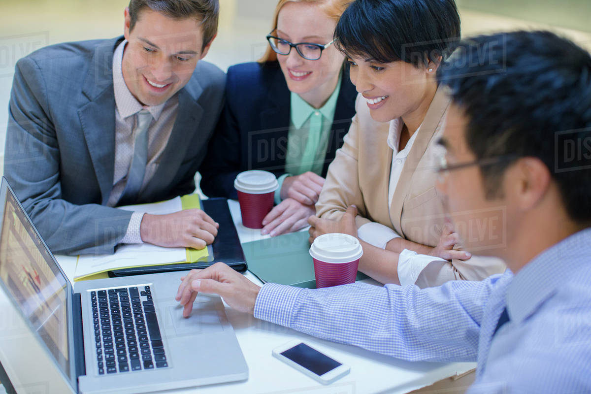 Business people gathered around laptop in office building cafe ...