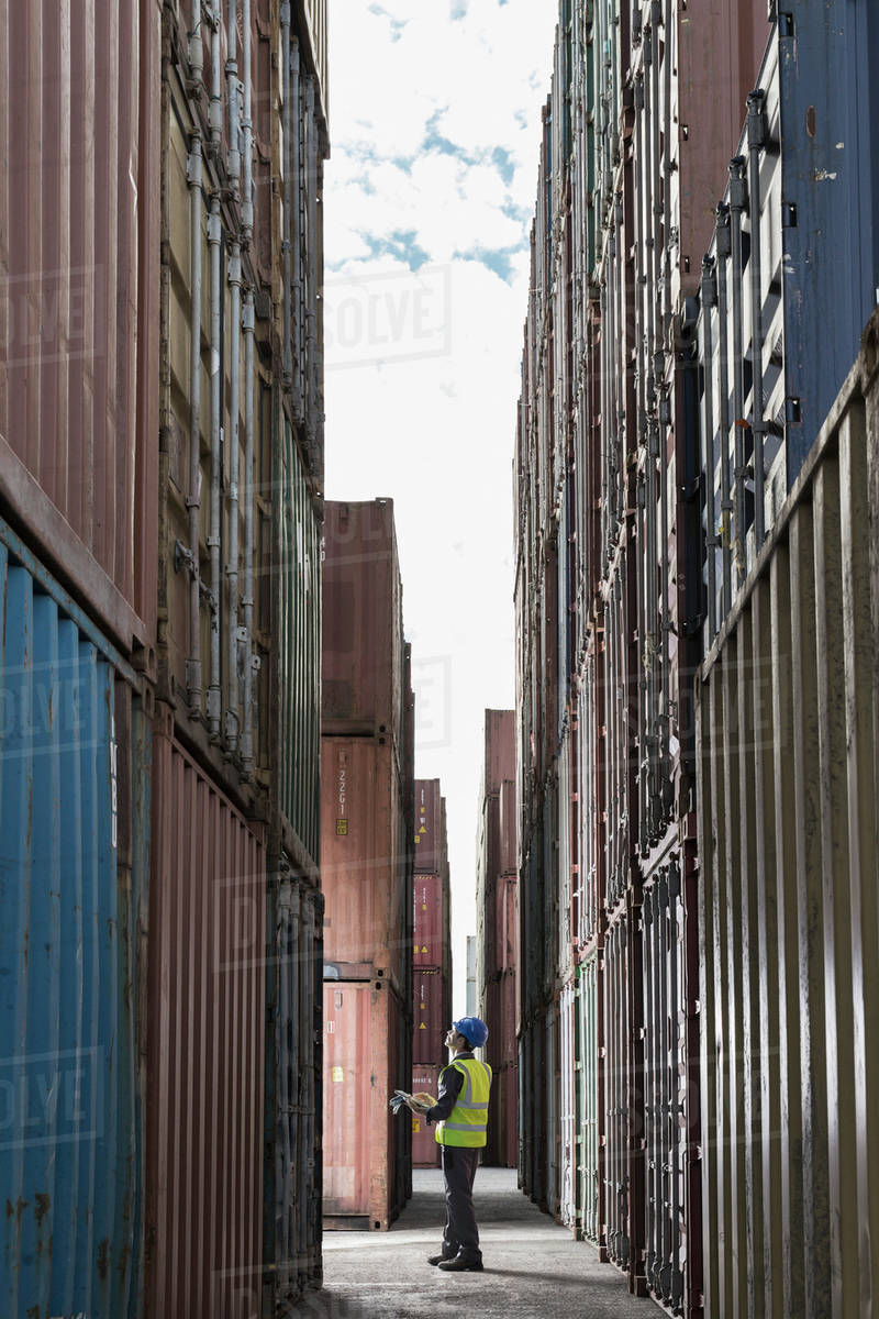 Worker standing between cargo containers - Stock Photo - Dissolve