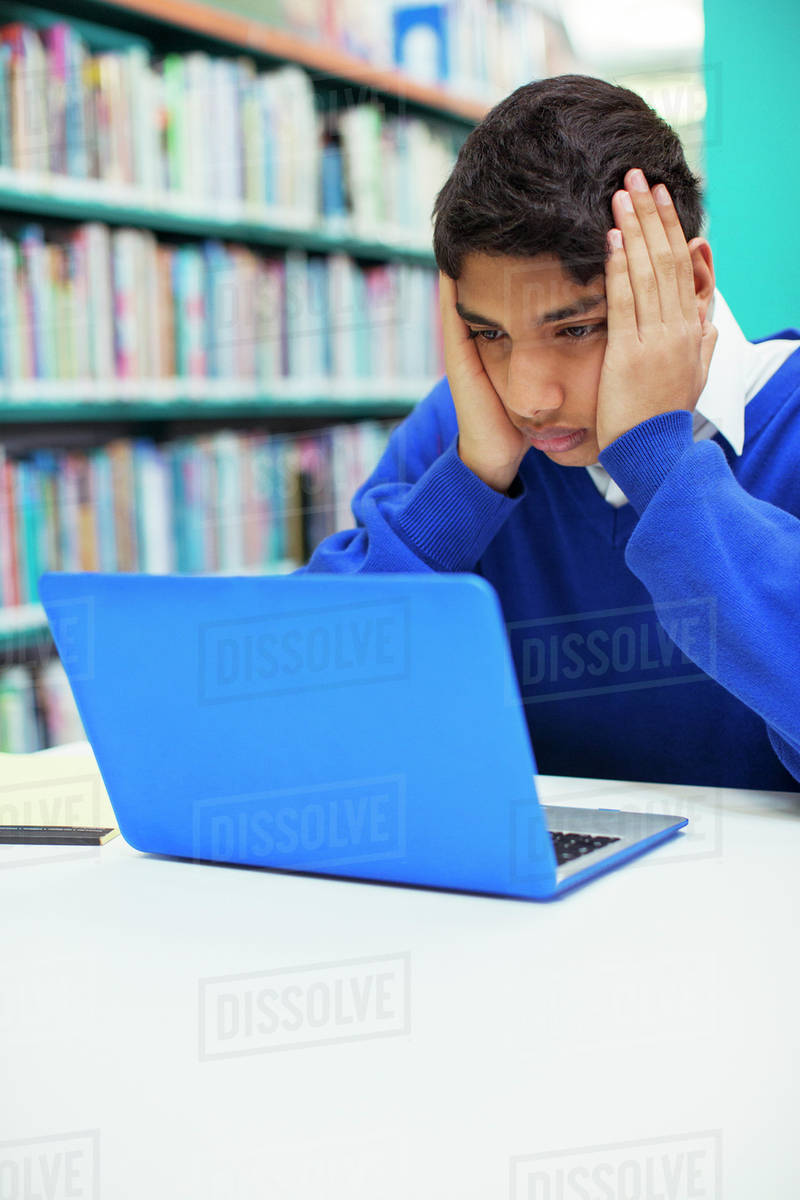 Portrait of worried student looking on laptop in library - Royalty-free ...