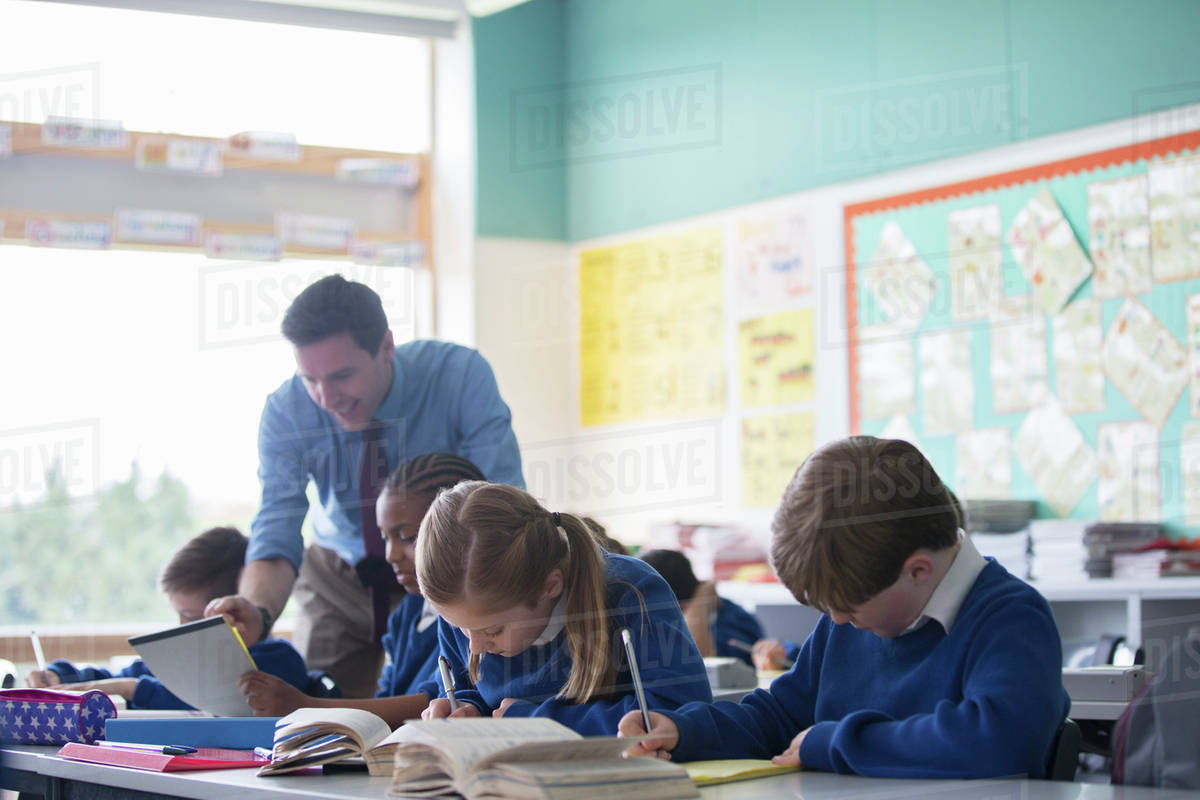 Male teacher assisting elementary school children in classroom during ...