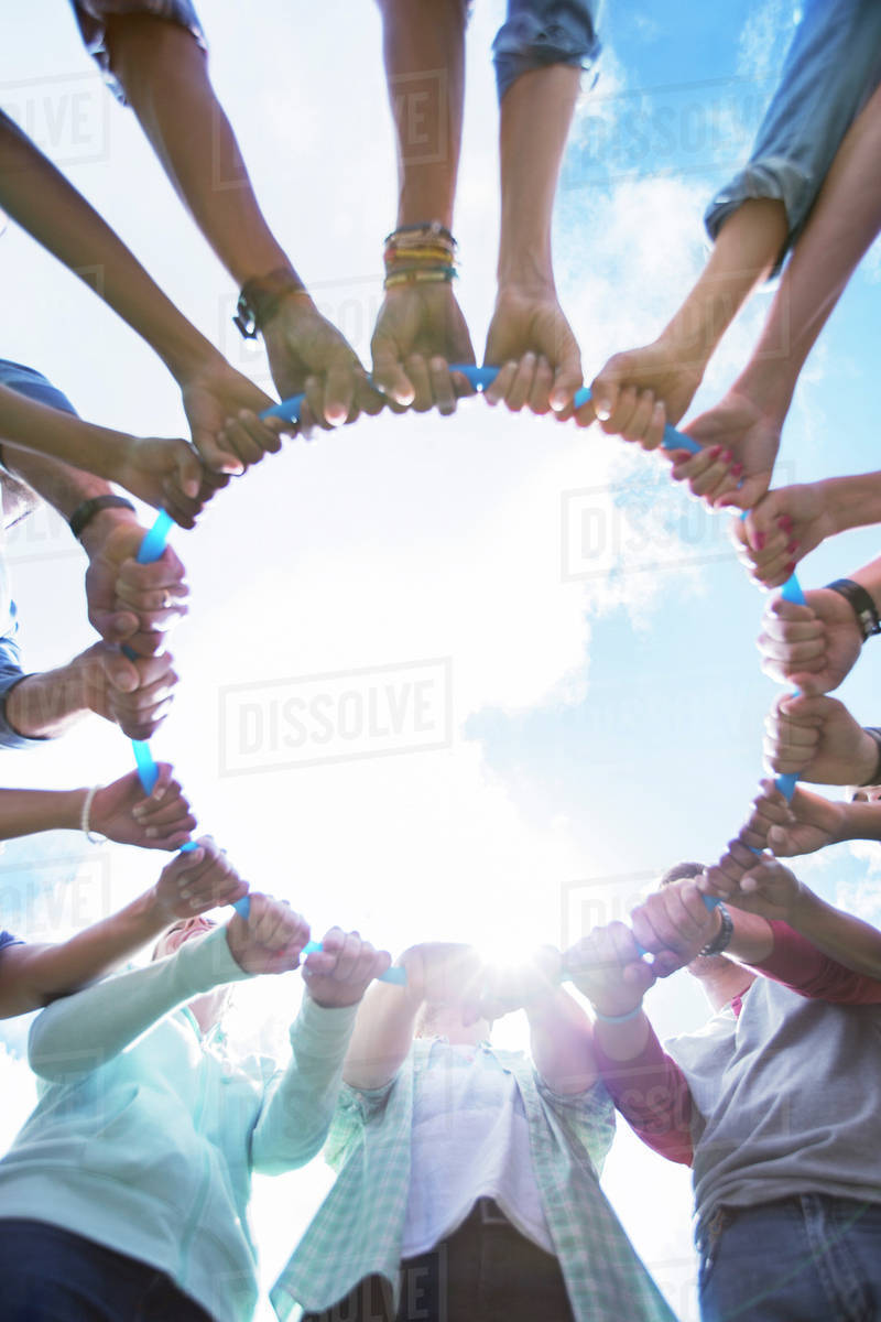 Team forming connected circle around plastic hoop - Stock Photo - Dissolve