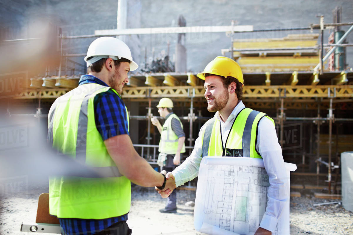 Construction worker and engineer with blueprints handshaking at ...