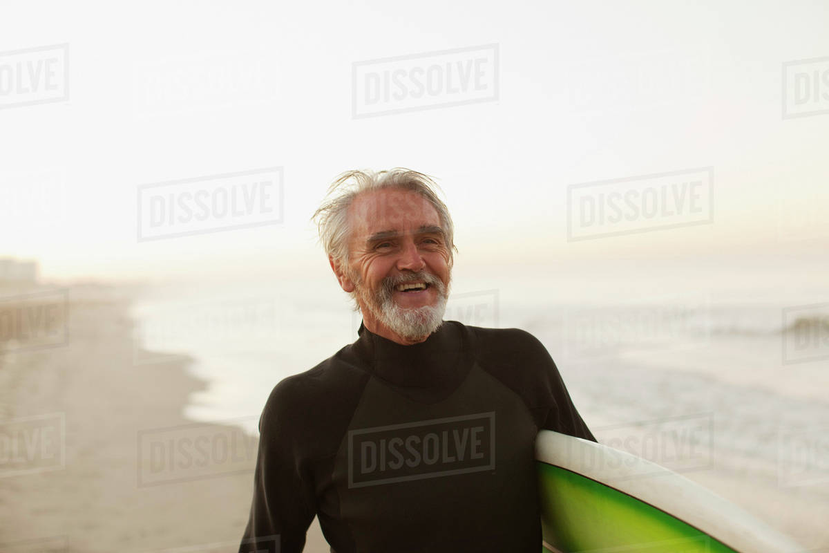 Older surfer carrying board on beach - Royalty-free Stock Photo | Dissolve