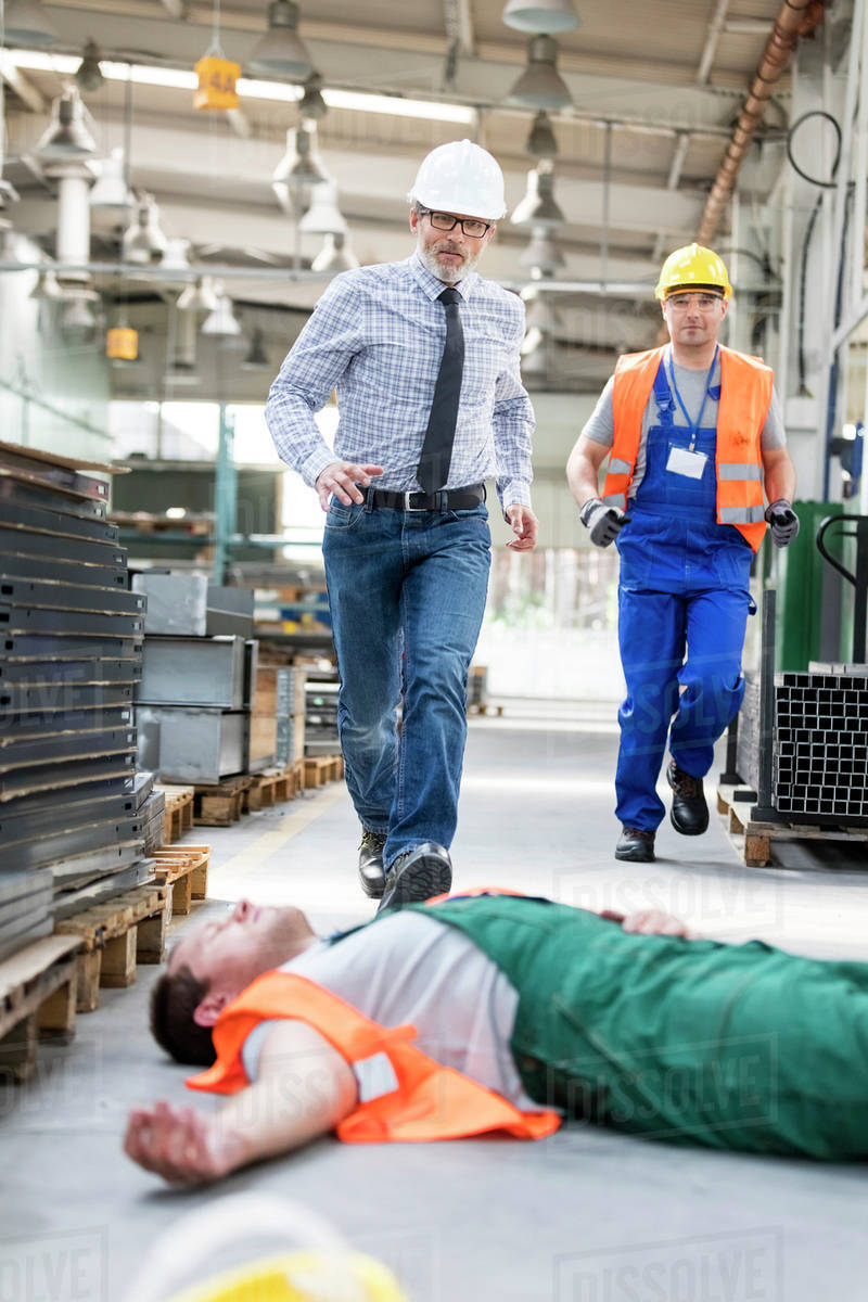 Workers running toward fallen coworker unconscious on factory floor ...