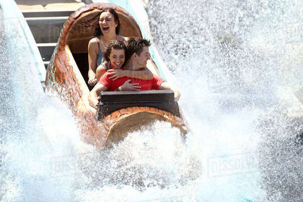 Enthusiastic friends getting splashed in water log amusement park ride ...