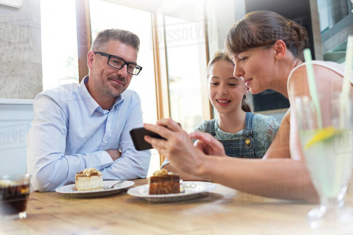 Family with cell phone eating dessert at cafe table - Royalty-free ...
