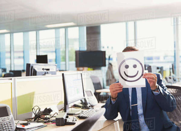 Portrait of businessman holding smiley face printout over his face in ...