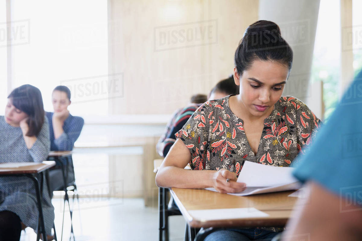 Serious female college student taking test at desk in classroom ...