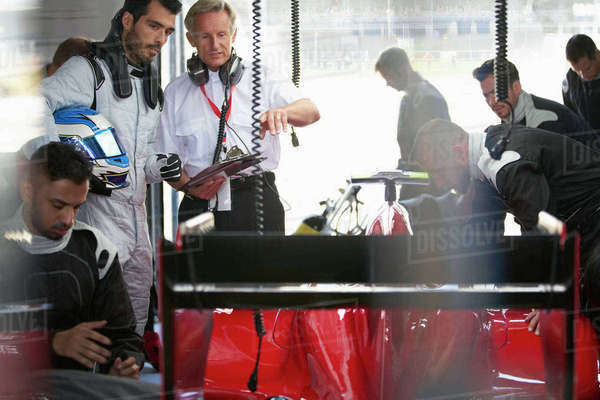 Manager and formula one driver watching pit crew working on race car in ...