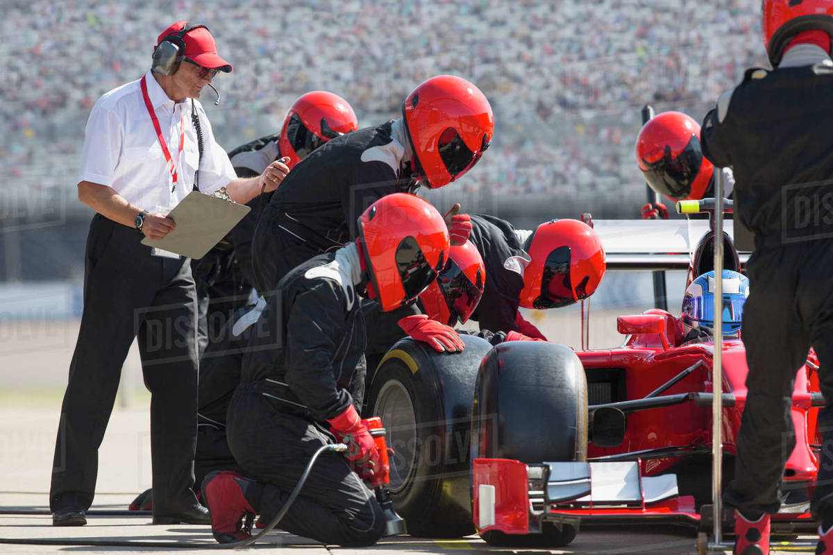 Manager with stopwatch timing pit crew replacing formula one race car ...