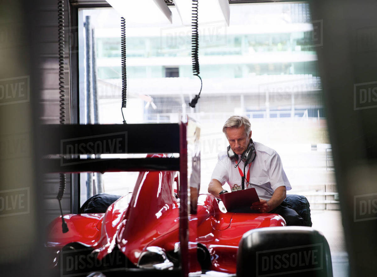 Manager with clipboard examining formula one race car in repair garage ...