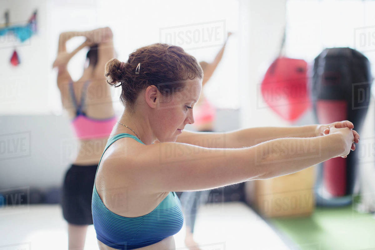 Focused female boxer stretching arms in gym - Stock Photo - Dissolve