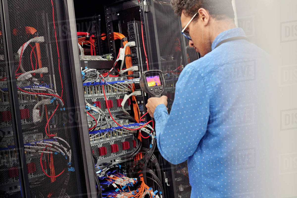 Male IT technician performing diagnostics on panel in server room ...
