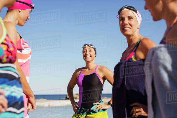 Smiling female open water swimmers wrapped din towels on sunny beach ...