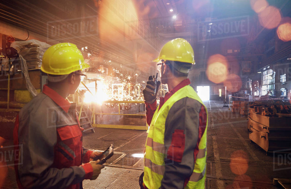 Steelworkers with walkie-talkie watching welding in steel mill ...
