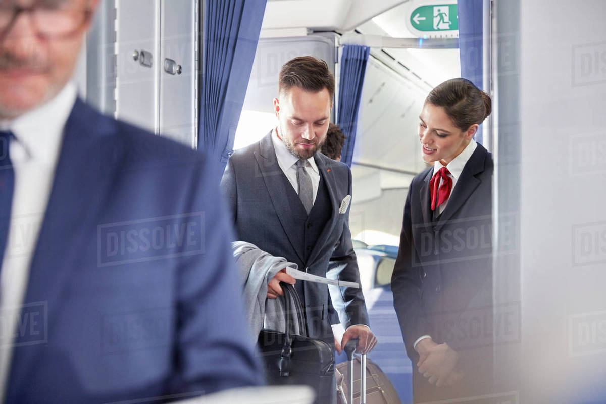 Flight attendant helping businessman with boarding pass on airplane ...