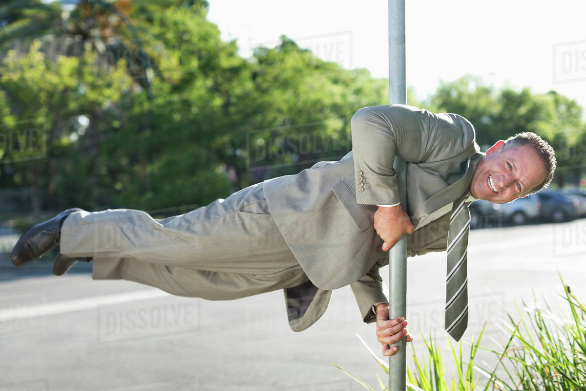 Businessman balancing on pole on city street - Stock Photo - Dissolve