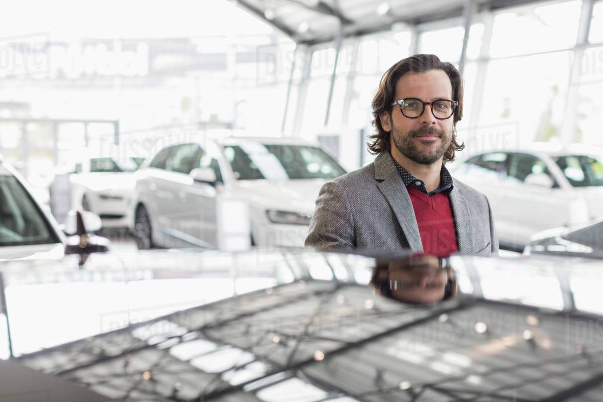 Portrait smiling, confident car salesman in car dealership showroom ...